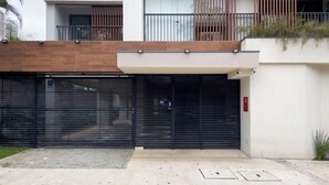 Um edifício moderno com uma porta de garagem fechada, uma varanda de madeira e uma parede branca com um sinal de saída de emergência vermelho.