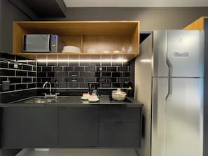 Cozinha moderna com micro-ondas, geladeira de aço inoxidável e painel de backsplash em azulejo preto.