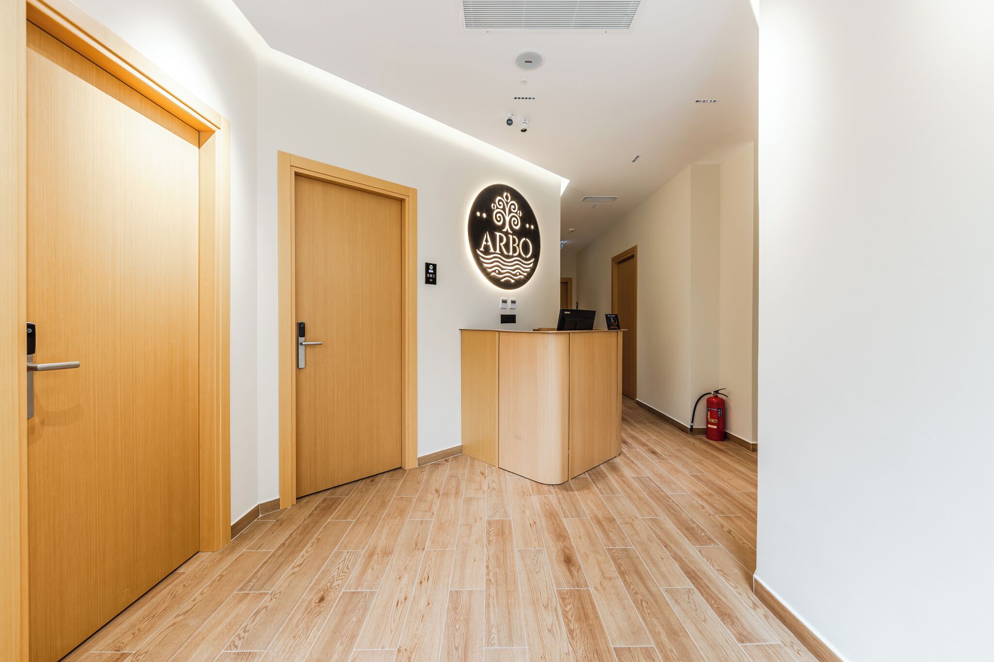Um corredor com portas de madeira, uma mesa de recepção com um logotipo e um extintor de incêndio.