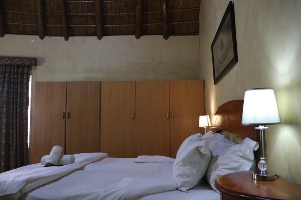 Quarto de hotel com uma cama, duas luminárias de cabeceira, um guarda-roupa de madeira e um quadro na parede.