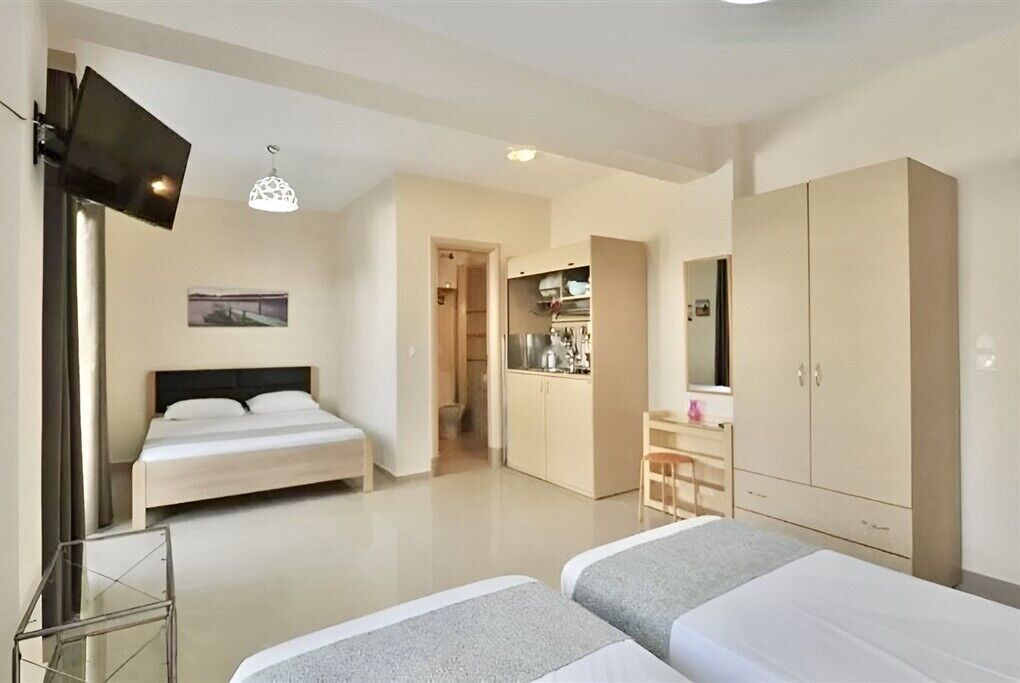 Quarto de hotel com duas camas, televisão, kitchenette e guarda-roupa.