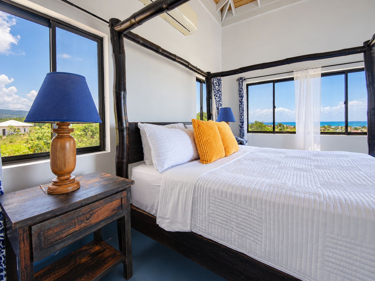 Quarto com cama de dossel, mesa de cabeceira e vista para o mar.