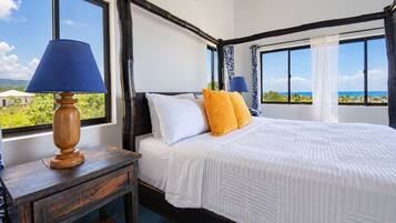 Quarto com cama de dossel, mesa de cabeceira e vista para o mar.