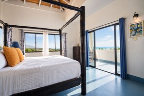 Uma cama com dossel com vista para o mar, uma varanda com uma cadeira e um quadro na parede.