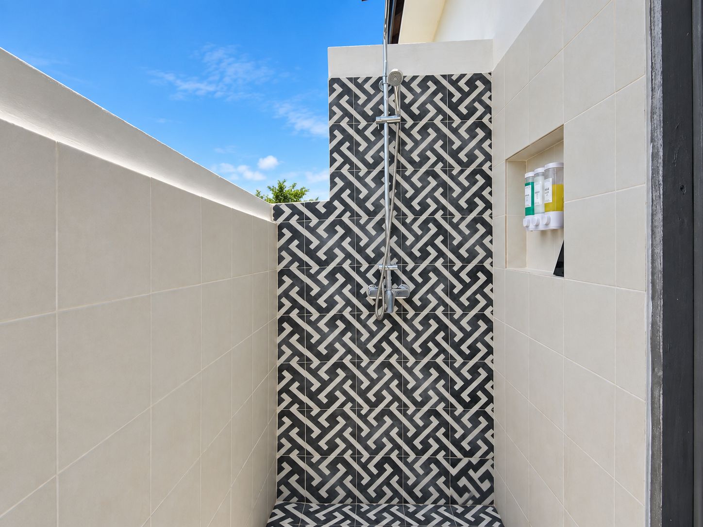 Casa de banho moderna com parede de chuveiro em padrão geométrico, secador de mãos à mão e pequena prateleira com produtos de higiene pessoal.