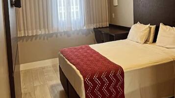 Quarto de hotel com uma cama, uma escrivaninha e uma cadeira.