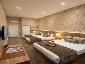Quarto de hotel com duas camas, uma televisão, uma mesa de centro de madeira e uma TV na parede.