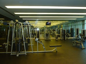 Uma academia com diversos aparelhos de exercício, uma tela de televisão e um espelho.