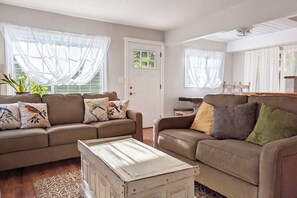 Uma sala de estar com dois sofás, uma mesa de centro e um espaço de refeições com cadeiras.