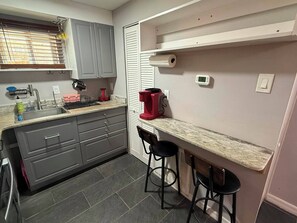 Cozinha compacta com pia, bancada e dois bancos.