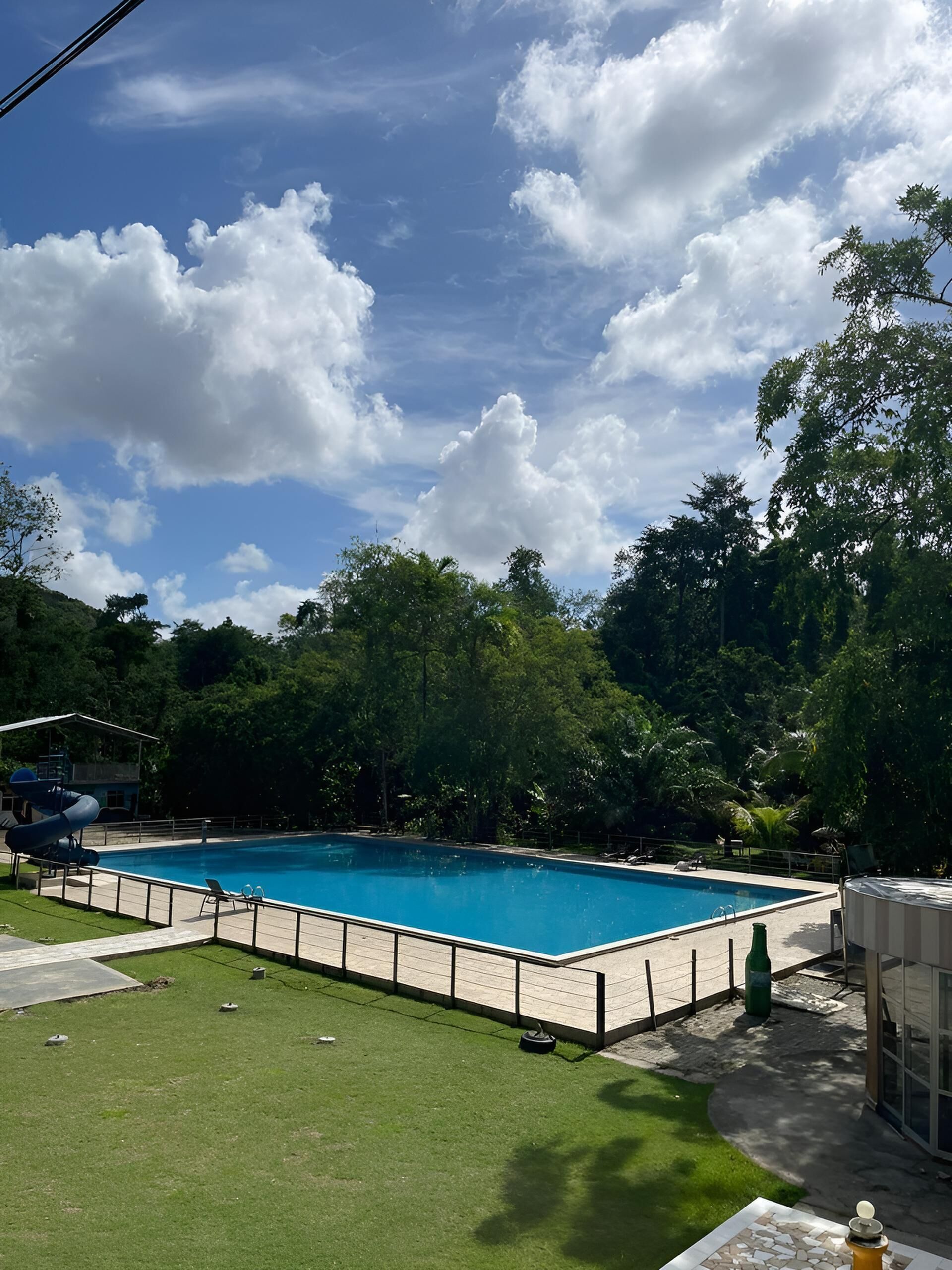 Piscina com escorregador, rodeada por vegetação exuberante e céu claro.