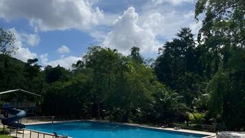 Piscina com escorregador, rodeada por vegetação exuberante e céu claro.