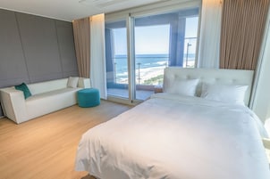 Quarto de hotel moderno com uma cama grande, um sofá e vista para a praia.