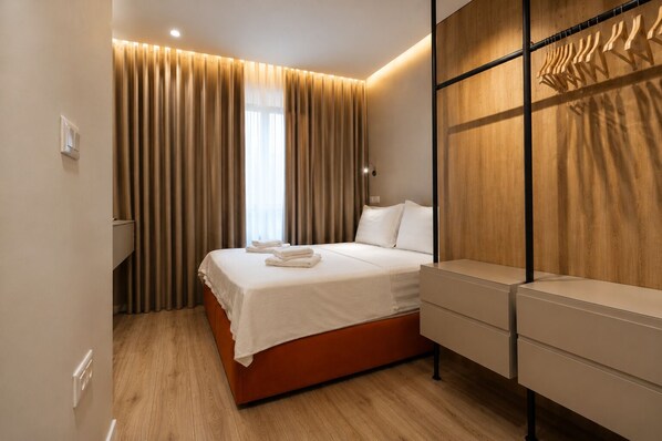 Quarto de hotel moderno com cama, mesas de cabeceira, cabeceira de madeira e janela com cortinas.