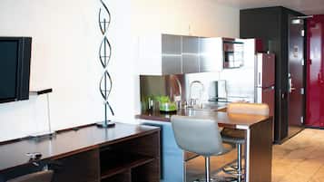 Cozinha moderna com ilha central, eletrodomésticos de aço inoxidável e TV de tela plana na parede.