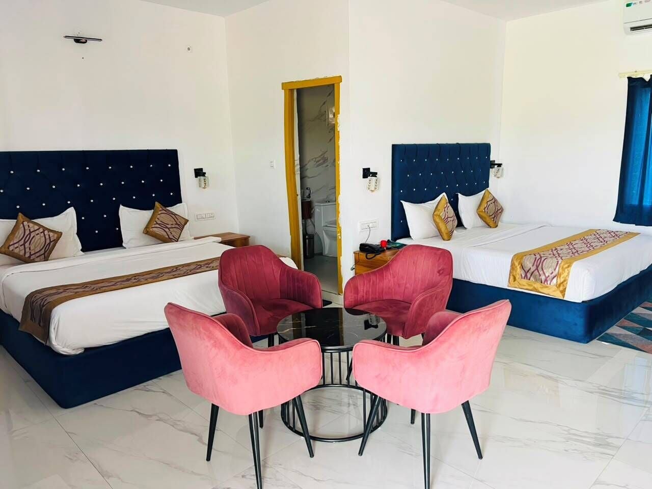 Quarto de hotel com duas camas, uma mesa redonda e duas cadeiras.