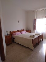Quarto com cama, mesas de cabeceira, luminária e janela com cortinas.