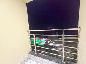 Uma varanda com grade de metal, vista para uma área iluminada em verde e um céu noturno escuro.