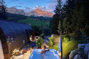Uma banheira de hidromassagem num jardim com vista para a montanha, um deck de madeira e uma casa.