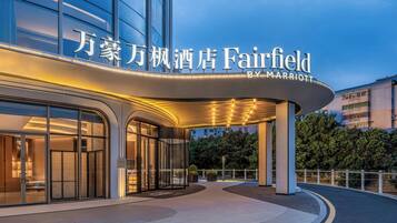 Entrada de hotel com design moderno, exibindo uma placa com o nome do hotel e um beiral curvo com iluminação.