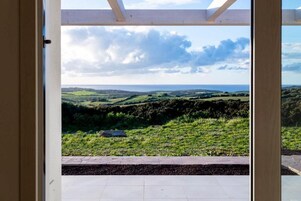 Vista através de uma porta para uma paisagem com colinas ondulantes e um horizonte distante.