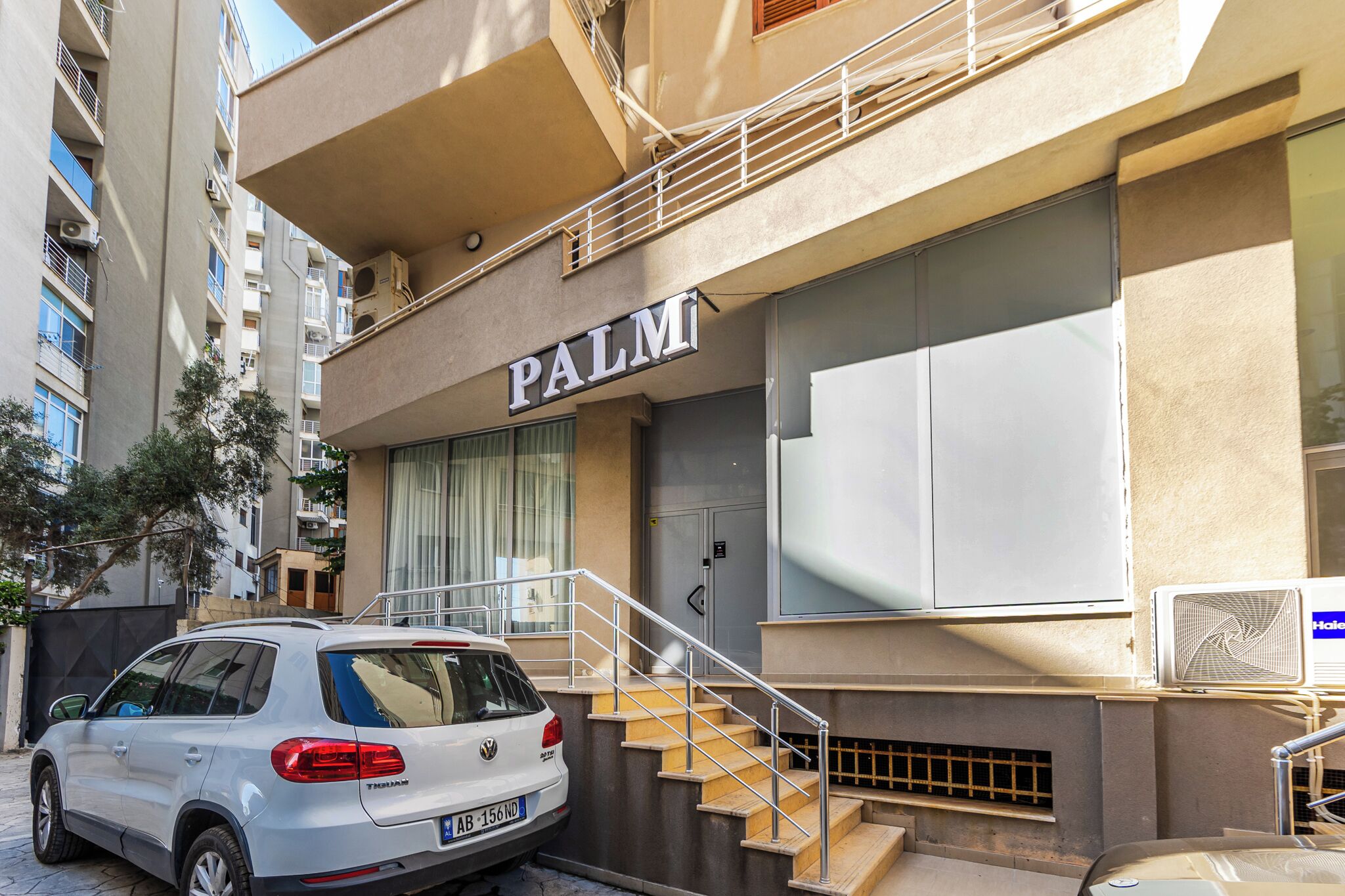Um edifício de vários andares com uma placa que diz 'PALMI' e um carro branco estacionado na frente.