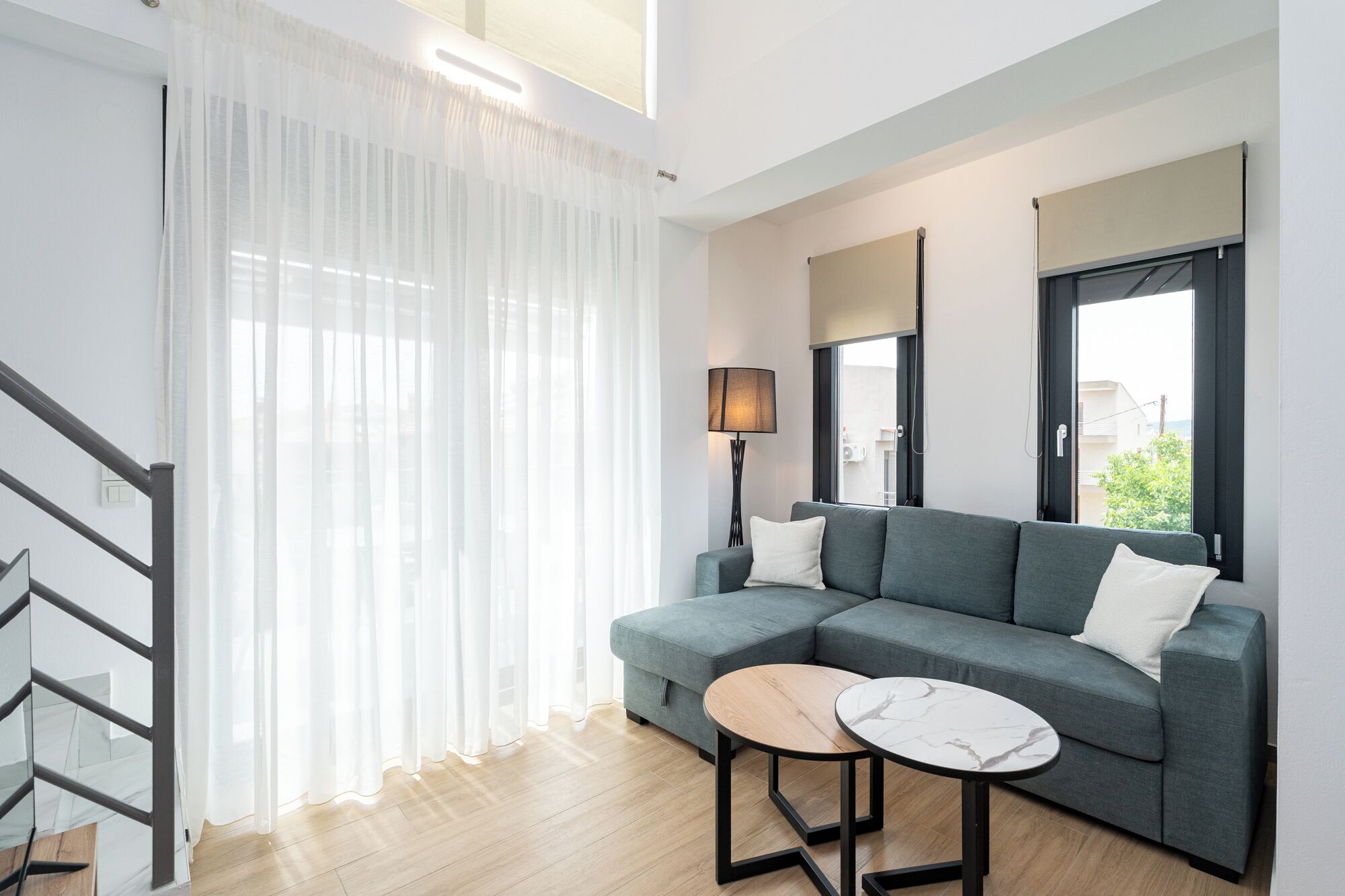 Uma sala de estar moderna com um sofá modular cinza, uma mesa de centro redonda, um abajur e uma escada.