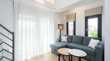 Uma sala de estar moderna com um sofá modular cinza, uma mesa de centro redonda, um abajur e uma escada.