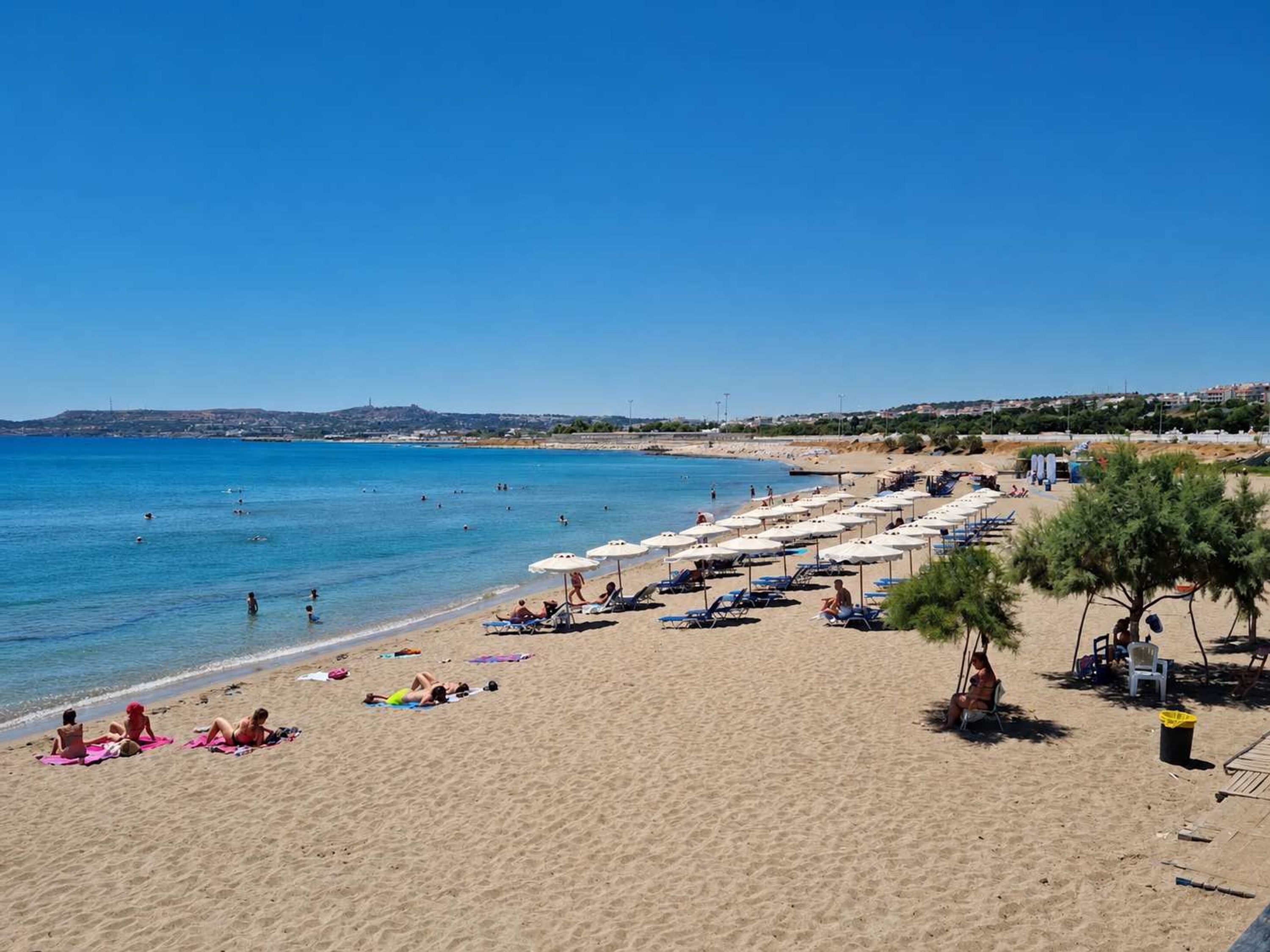 Uma praia com espreguiçadeiras e guarda-sóis, uma faixa de areia e um mar azul e límpido.