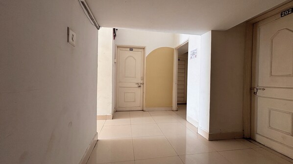 Um corredor com portas brancas, uma delas marcada com o número 205, que leva a um quarto com parede bege.