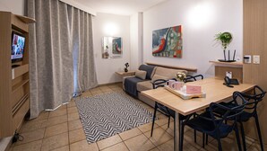 Uma sala de estar moderna com um sofá, uma mesa de centro e uma televisão. Há uma área de refeições com uma mesa e cadeiras.