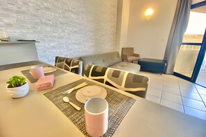 Uma sala de estar moderna com um sofá, uma mesa de jantar posta com pratos, xícaras e talheres, e um vaso de planta.