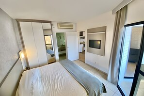 Quarto de hotel moderno com uma cama grande, uma televisão fixada na parede e uma porta deslizante para um banheiro.