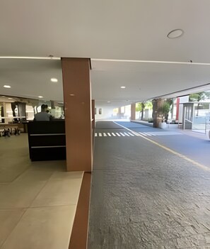 Um saguão amplo com uma mesa de recepção, uma faixa de pedestres que leva a uma área externa e um pilar grande.