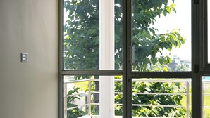 Quarto com uma grande janela, parede branca e guarda-corpo de varanda visível.