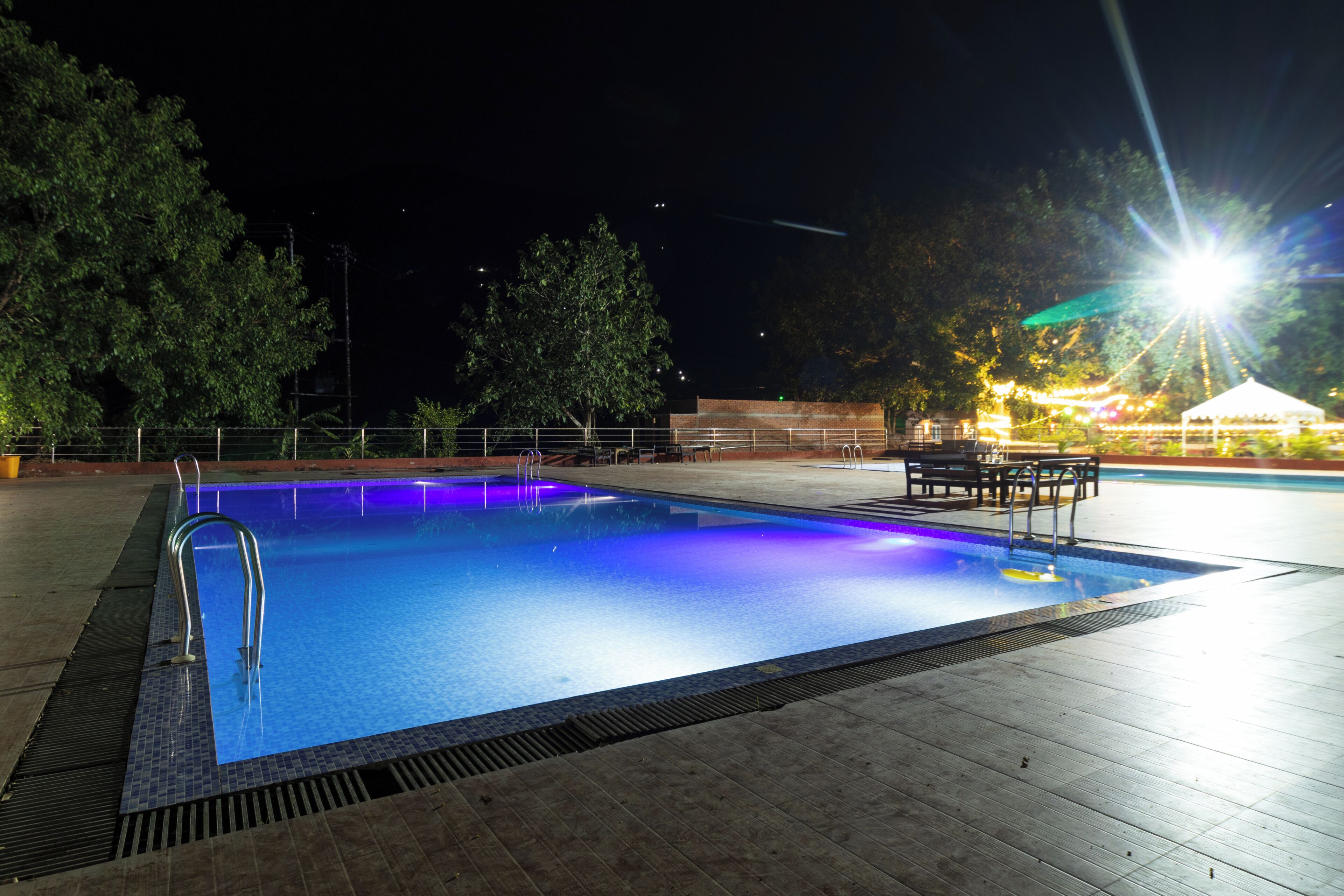 Uma piscina com uma escada de metal, rodeada por um deck revestido e uma cerca.