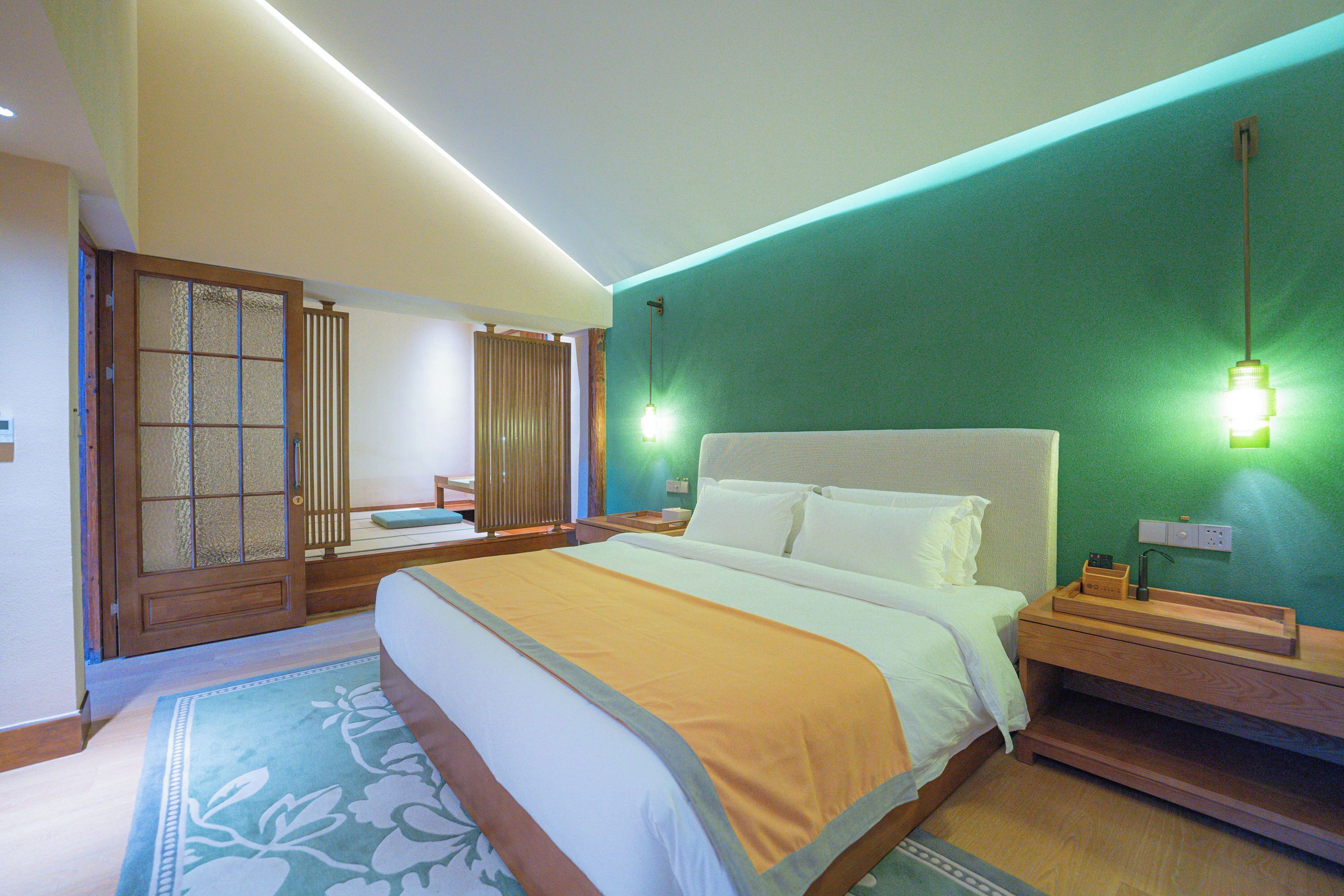 Quarto de hotel com cama, mesas de cabeceira, um piso de madeira e uma parede verde decorativa.