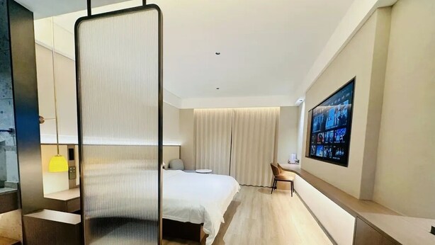 Quarto de hotel moderno com cama, escrivaninha, cadeira, televisão e uma grande janela.