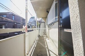 Uma varanda estreita com grade de metal, uma porta e vista para edifícios vizinhos.
