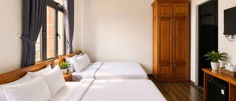 Quarto de hotel com duas camas, um guarda-roupa, uma televisão e uma pequena mesa com uma planta.