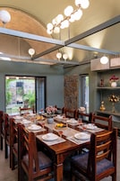 Uma sala de jantar com uma longa mesa de madeira posta para uma refeição, rodeada por cadeiras.