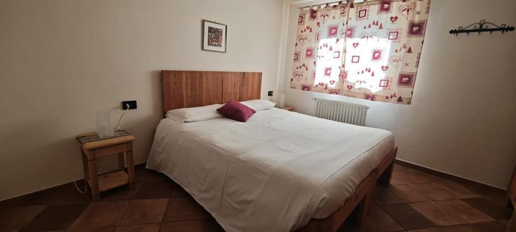 Um quarto com uma cama, uma mesa de cabeceira, um radiador e uma janela com cortinas.