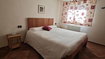Um quarto com uma cama, uma mesa de cabeceira, um radiador e uma janela com cortinas.