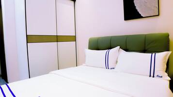 Cama com roupa de cama branca e cabeceira verde, parede branca com uma obra de arte emoldurada e porta com design verde e branco.