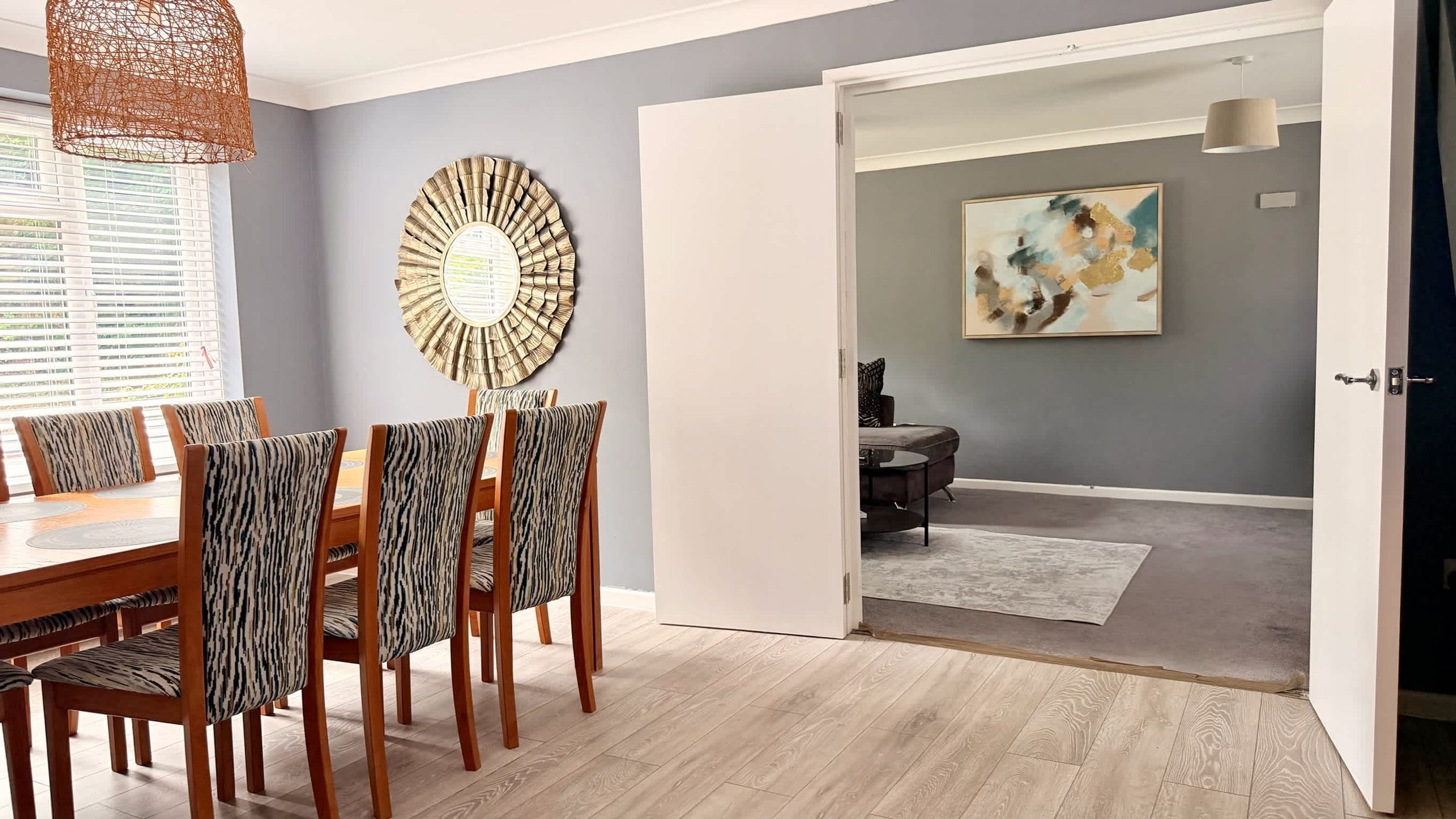 Uma área de refeições com um espelho redondo, uma mesa de jantar com cadeiras e um quadro na parede.