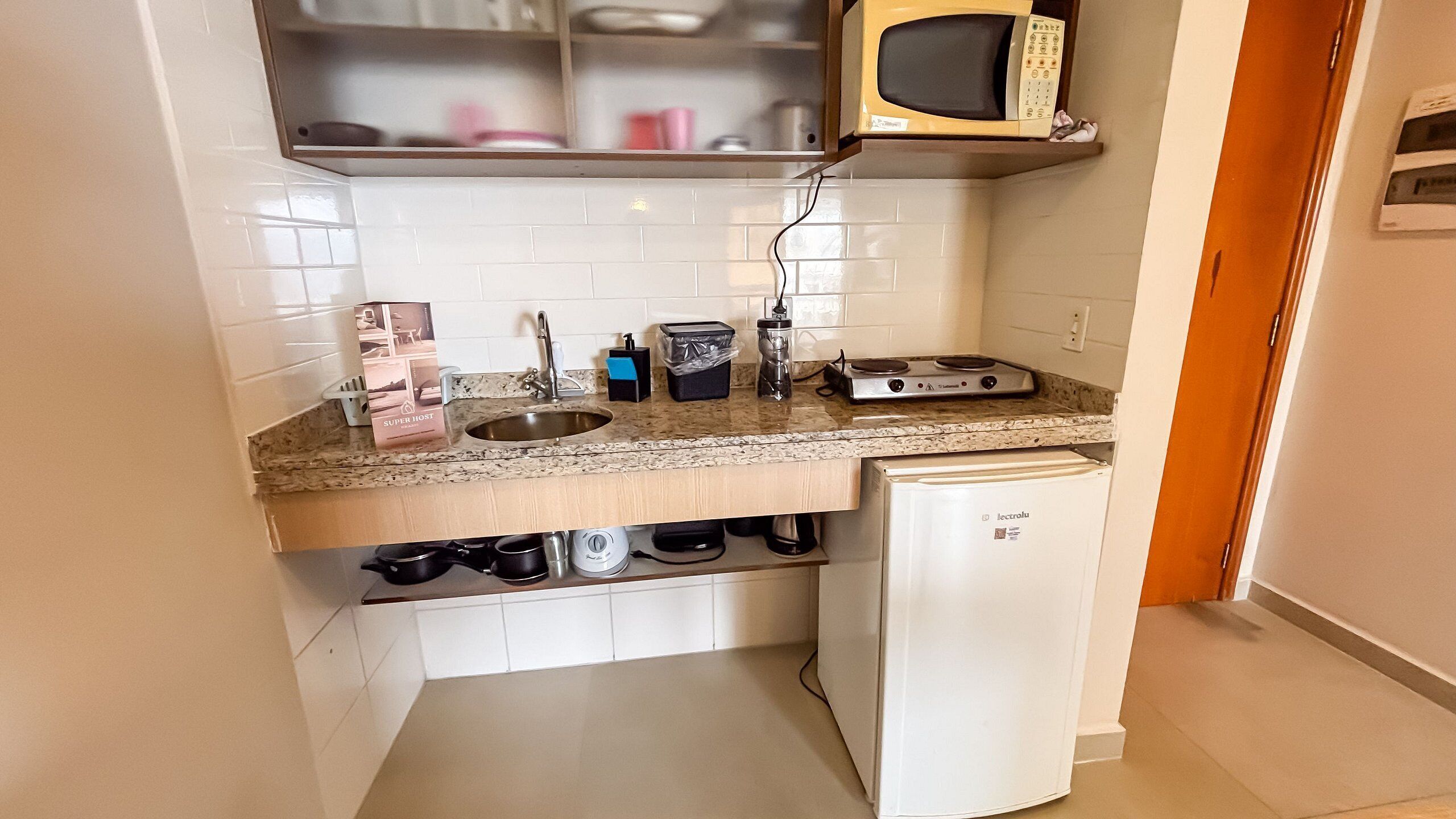 Uma cozinha compacta com pia, micro-ondas, torradeira e geladeira.