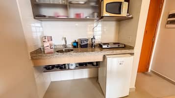 Uma cozinha compacta com pia, micro-ondas, torradeira e geladeira.
