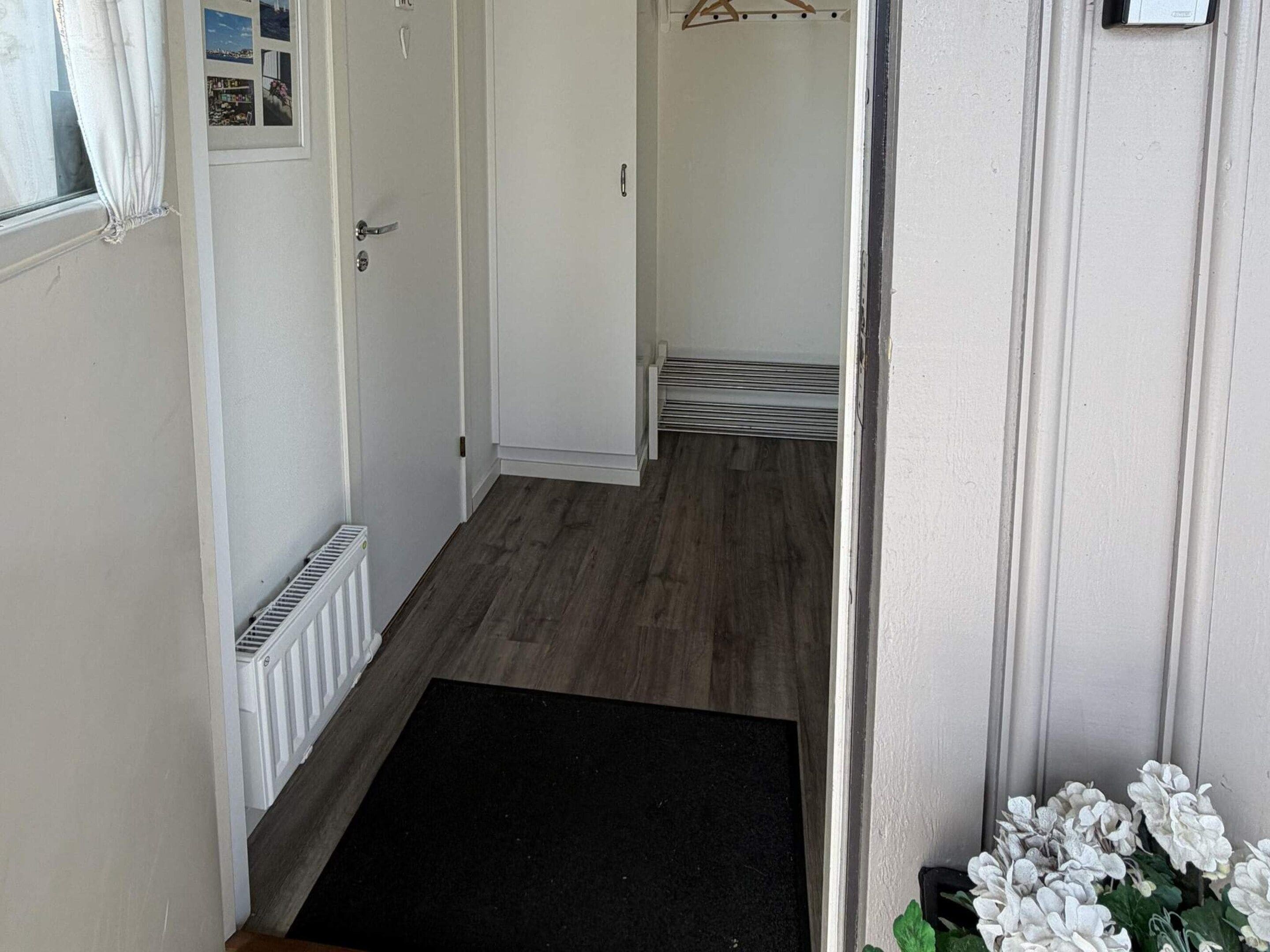 Um corredor com um radiador, um tapete preto na entrada e uma porta com cabides.
