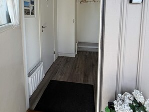 Um corredor com um radiador, um tapete preto na entrada e uma porta com cabides.