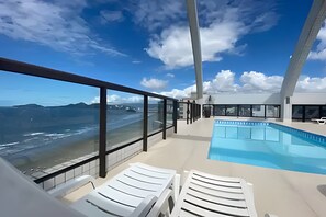 Área de piscina moderna no terraço, com vista clara para o oceano e montanhas.